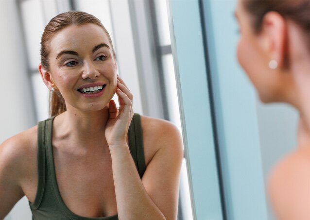 A woman wearing a green tank top smiles as she touches her smooth skin ...
