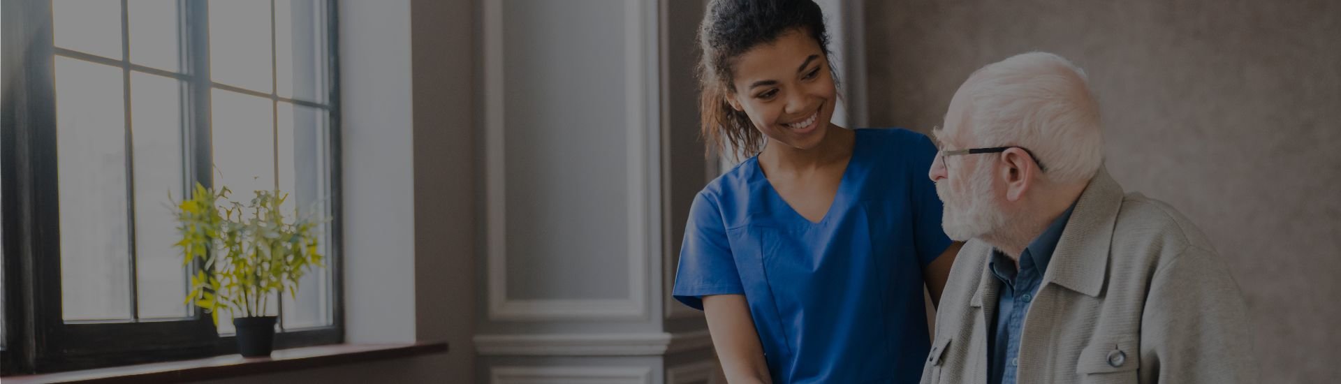 Cross Country color photo of a female nurse in blue scrubs smiling at an elderly patient.